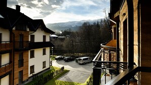 Edifício residencial com varanda que oferece vista para um estacionamento e uma paisagem montanhosa.