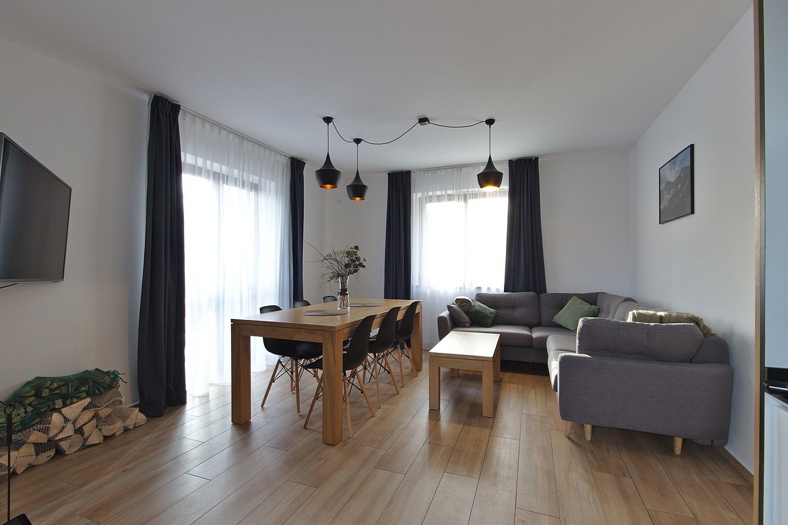 Uma sala de estar moderna com uma mesa de jantar de madeira, um sofá e uma TV na parede.
