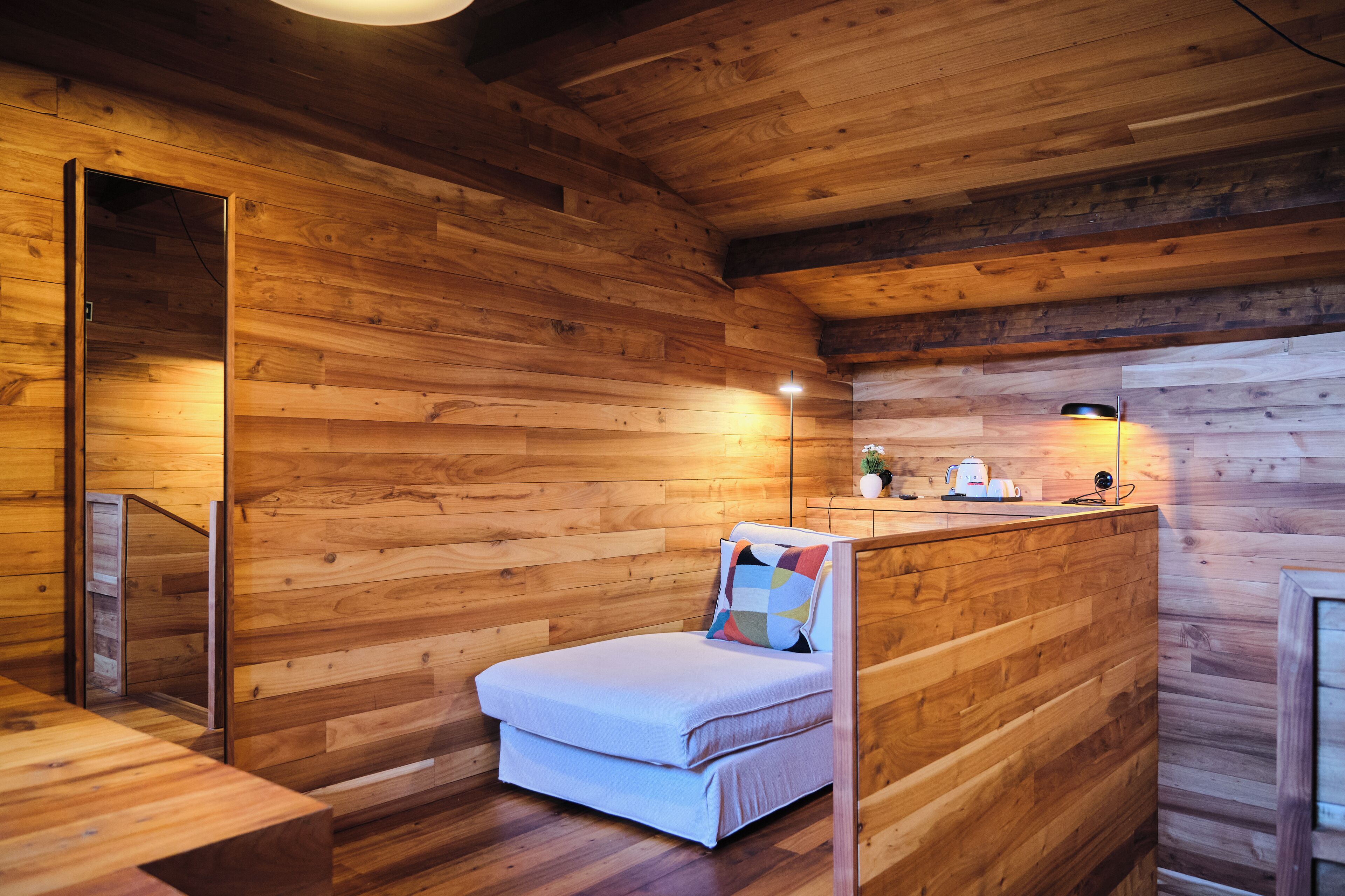 Interior de uma cabana de madeira com uma cama, uma mesa pequena e uma mesinha de cabeceira.