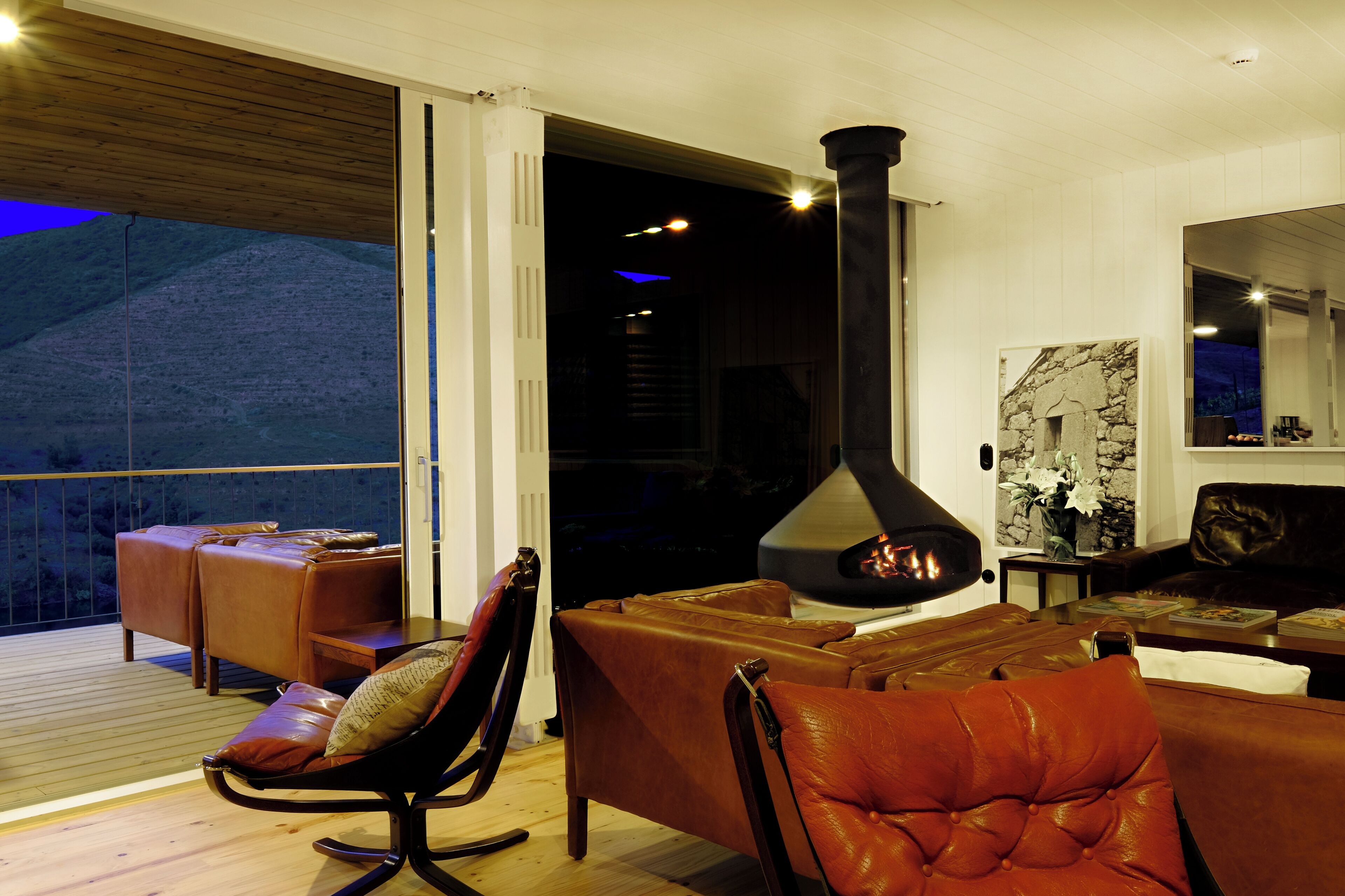 Uma sala de estar moderna com sofás de couro, uma lareira e vista para uma paisagem montanhosa.