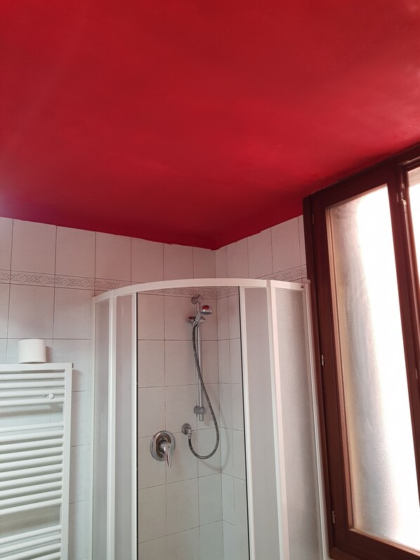 Chuveiro com porta de vidro, paredes azulejadas em branco e teto vermelho.