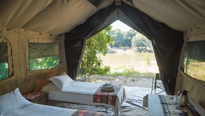 Acomodação em tenda com duas camas, uma mesa com chaleira, e vista para um rio e árvores.