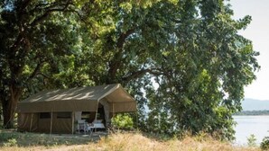 Alojamento em tenda junto a um lago, com vista para a água e montanhas ao longe.