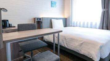 Quarto de hotel com cama, escrivaninha, cadeira, cafeteira e relógio de parede.