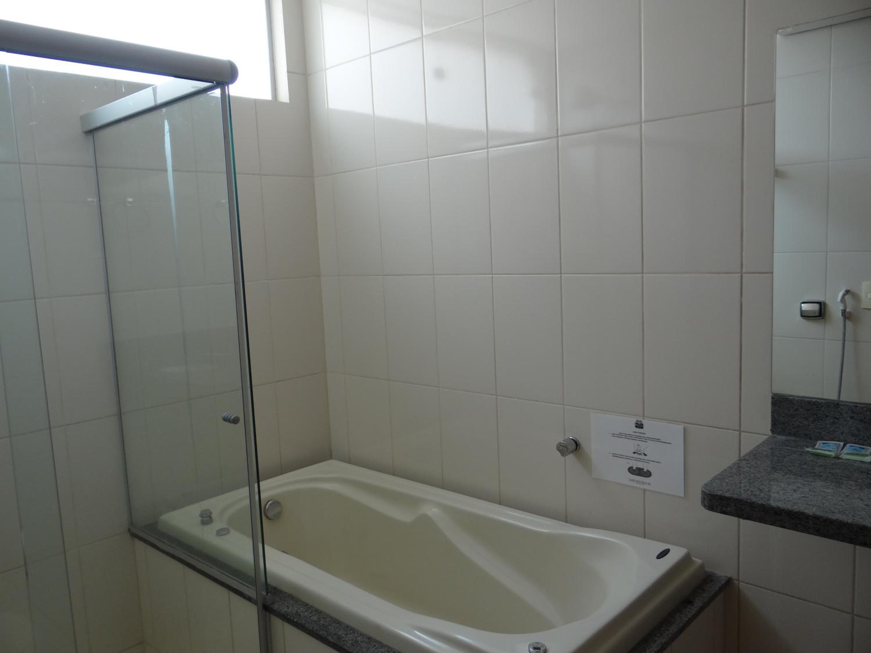 Uma casa de banho com cabine de duche em vidro, banheira e bancada de granito com dispensador de sabonete.