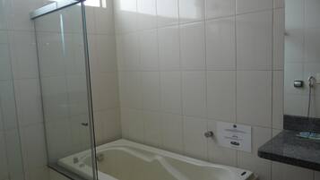 Uma casa de banho com cabine de duche em vidro, banheira e bancada de granito com dispensador de sabonete.
