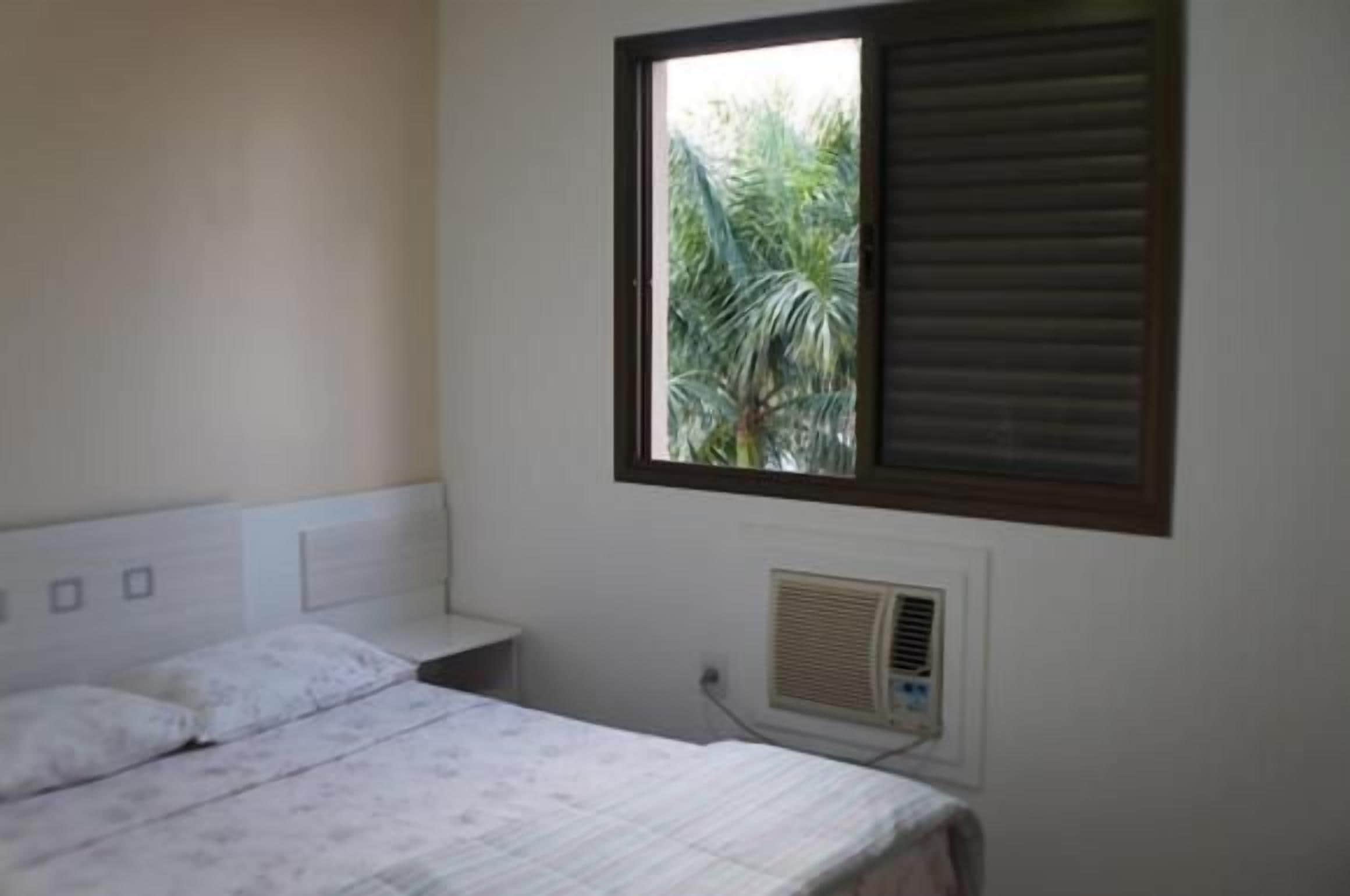 Quarto com uma cama, janela e ar-condicionado fixado na parede.