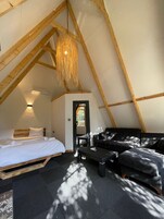 Um quarto loft aconchegante com uma cama, um sofá de couro preto, uma mesinha e um pendente.