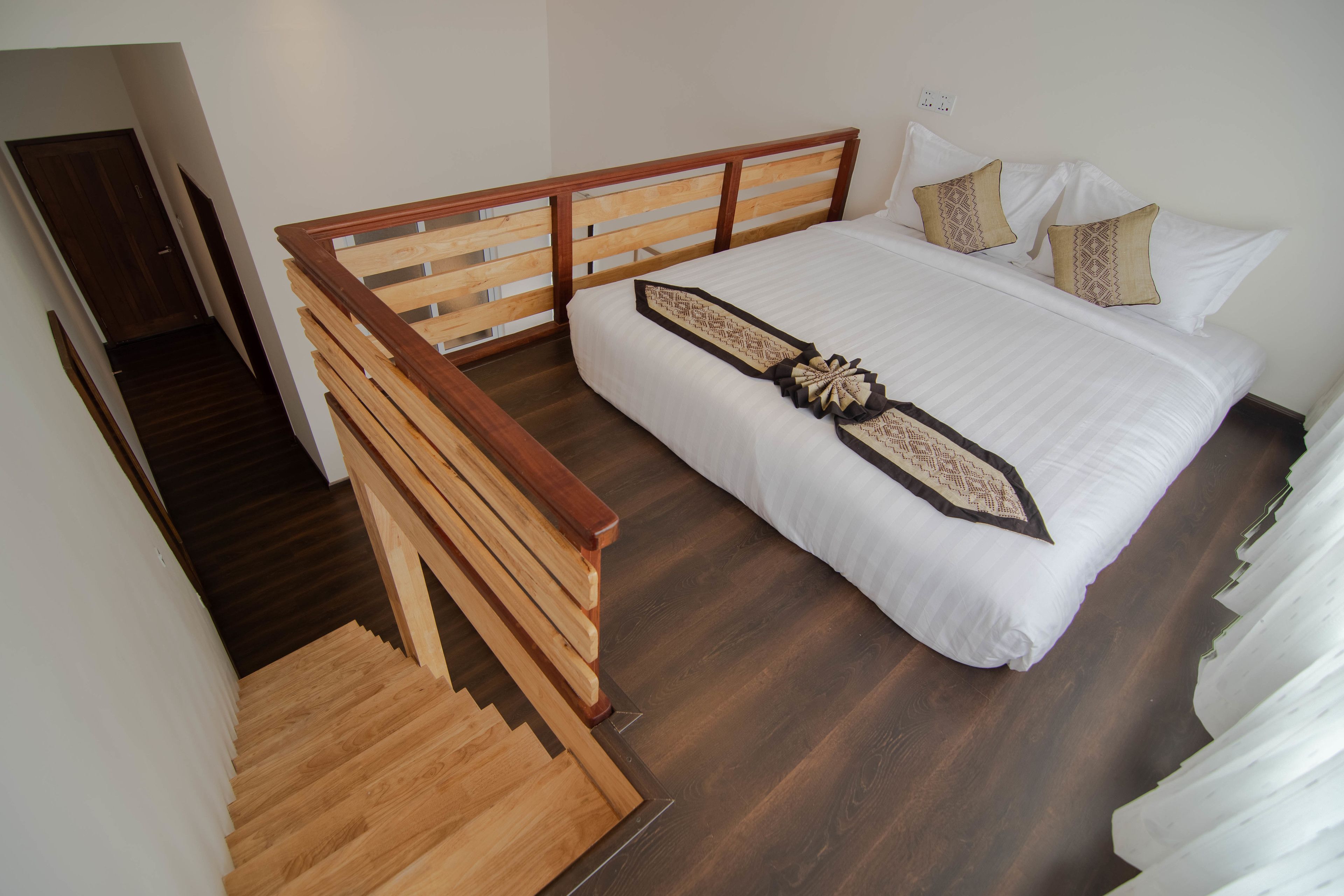 Quarto com cabeceira de madeira, cama grande com roupa de cama branca e escada que leva a um andar superior.