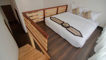 Quarto com cabeceira de madeira, cama grande com roupa de cama branca e escada que leva a um andar superior.
