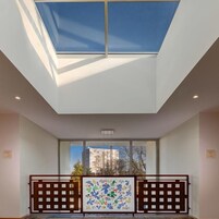 Quarto com claraboia, grandes janelas e vista para edifícios.