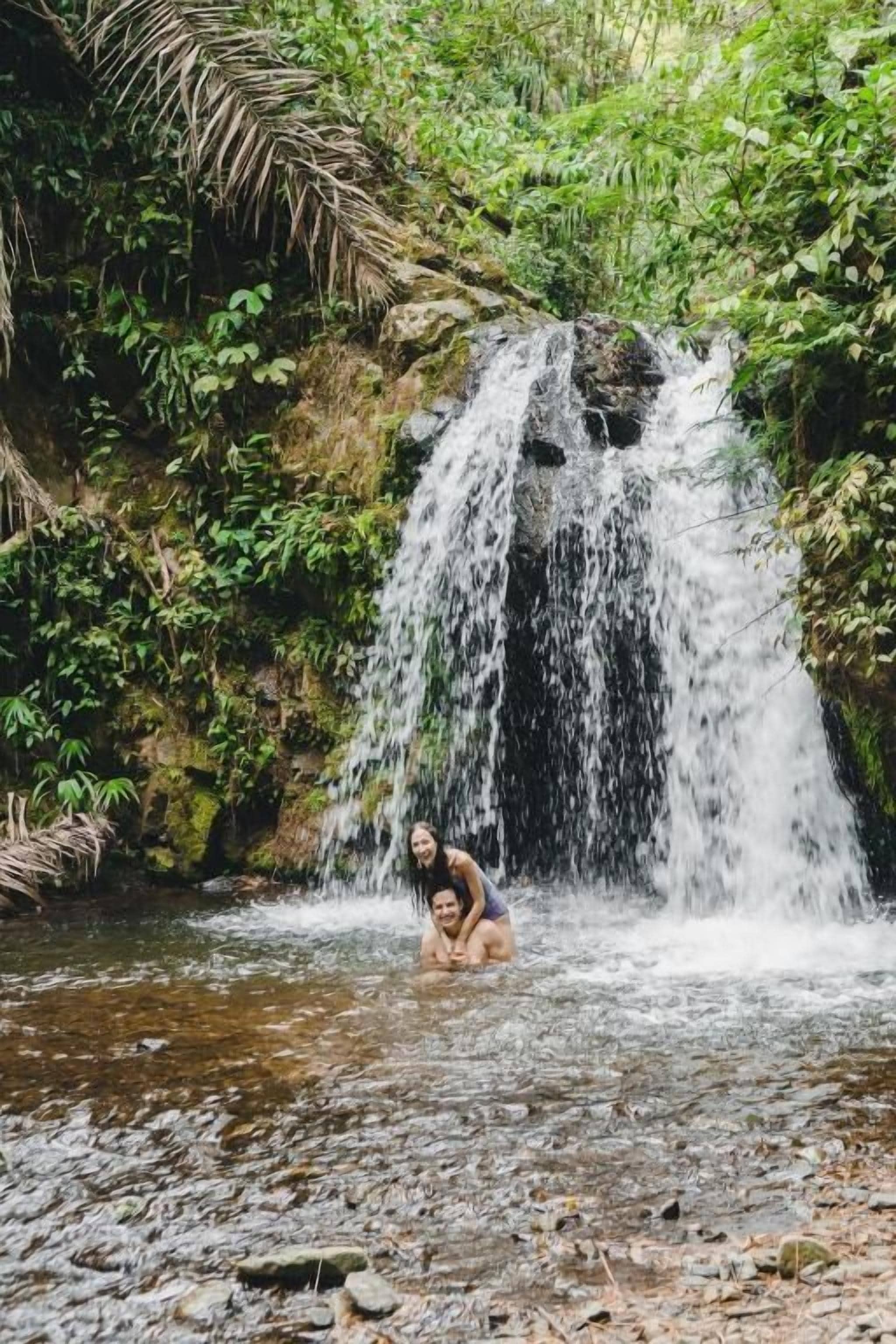 Uma cascata em ambiente natural, com uma pessoa na água.