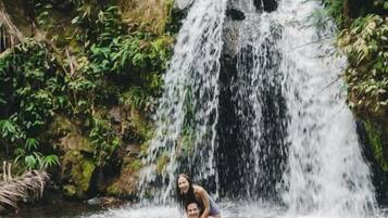 Uma cascata em ambiente natural, com uma pessoa na água.