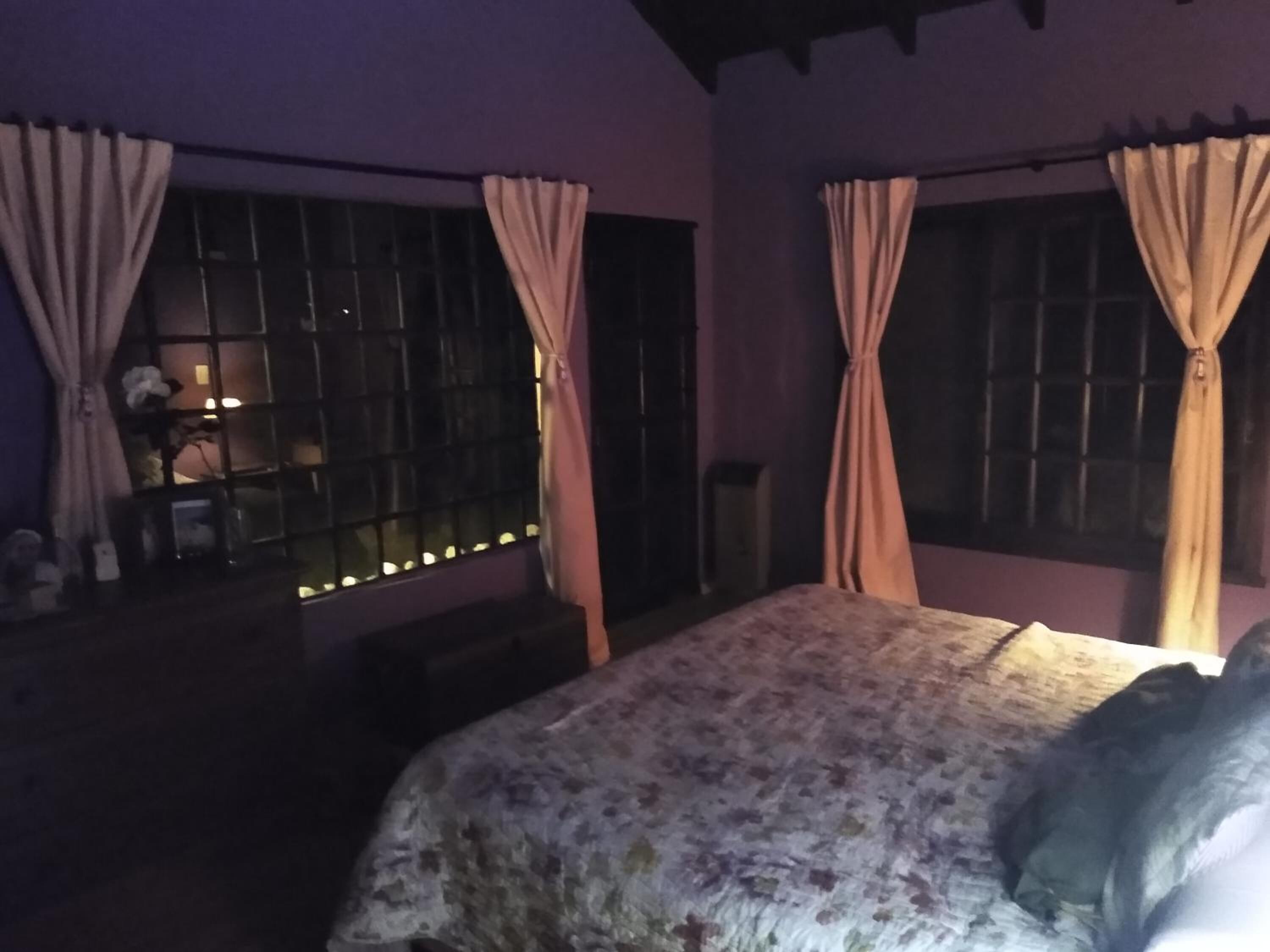 Um quarto com pouca luz, com uma cama, um penteado e duas janelas com cortinas.