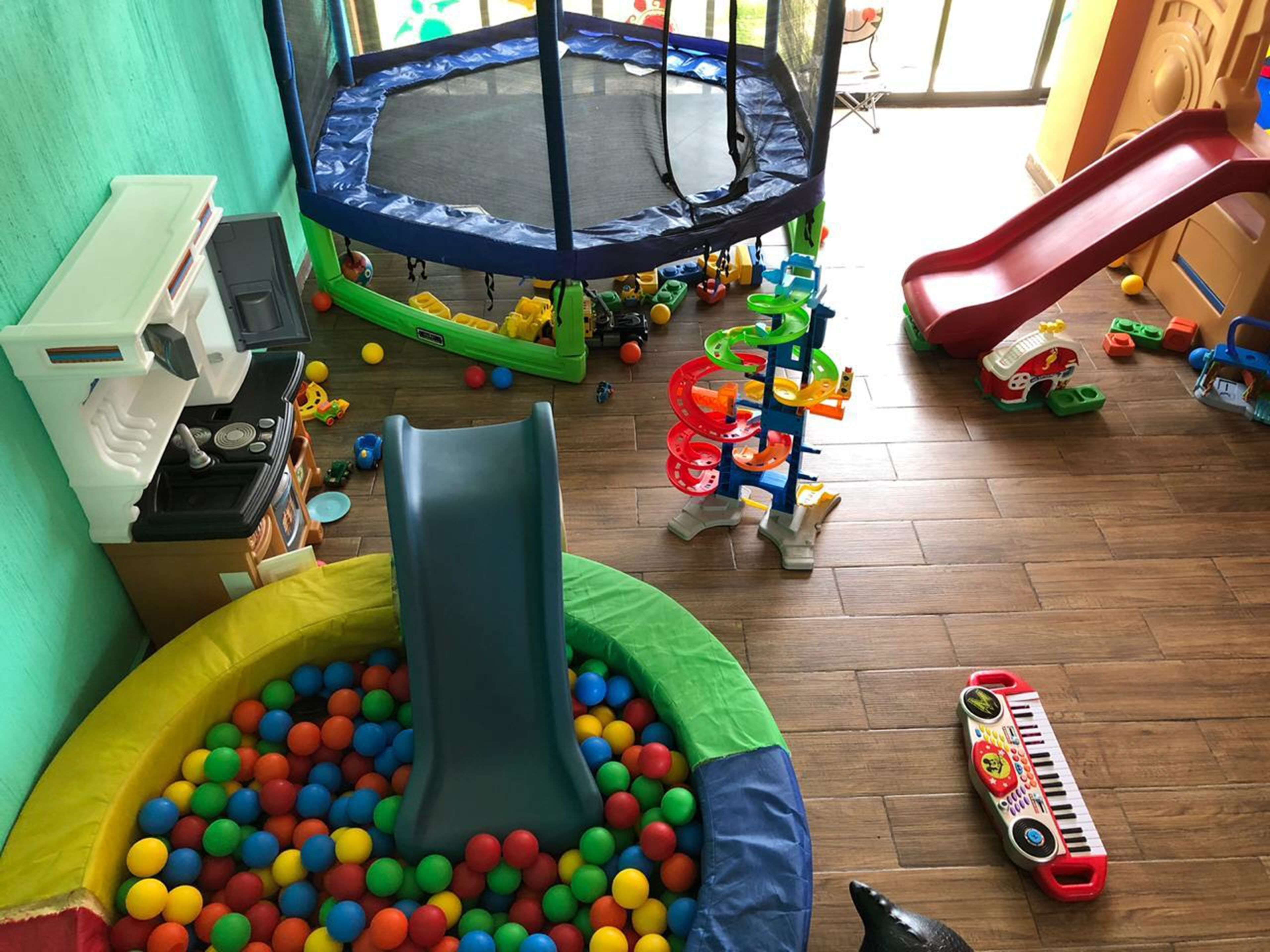Um espaço de recreação com um trampolim, um escorrega, uma piscina de bolinhas e diversos brinquedos.