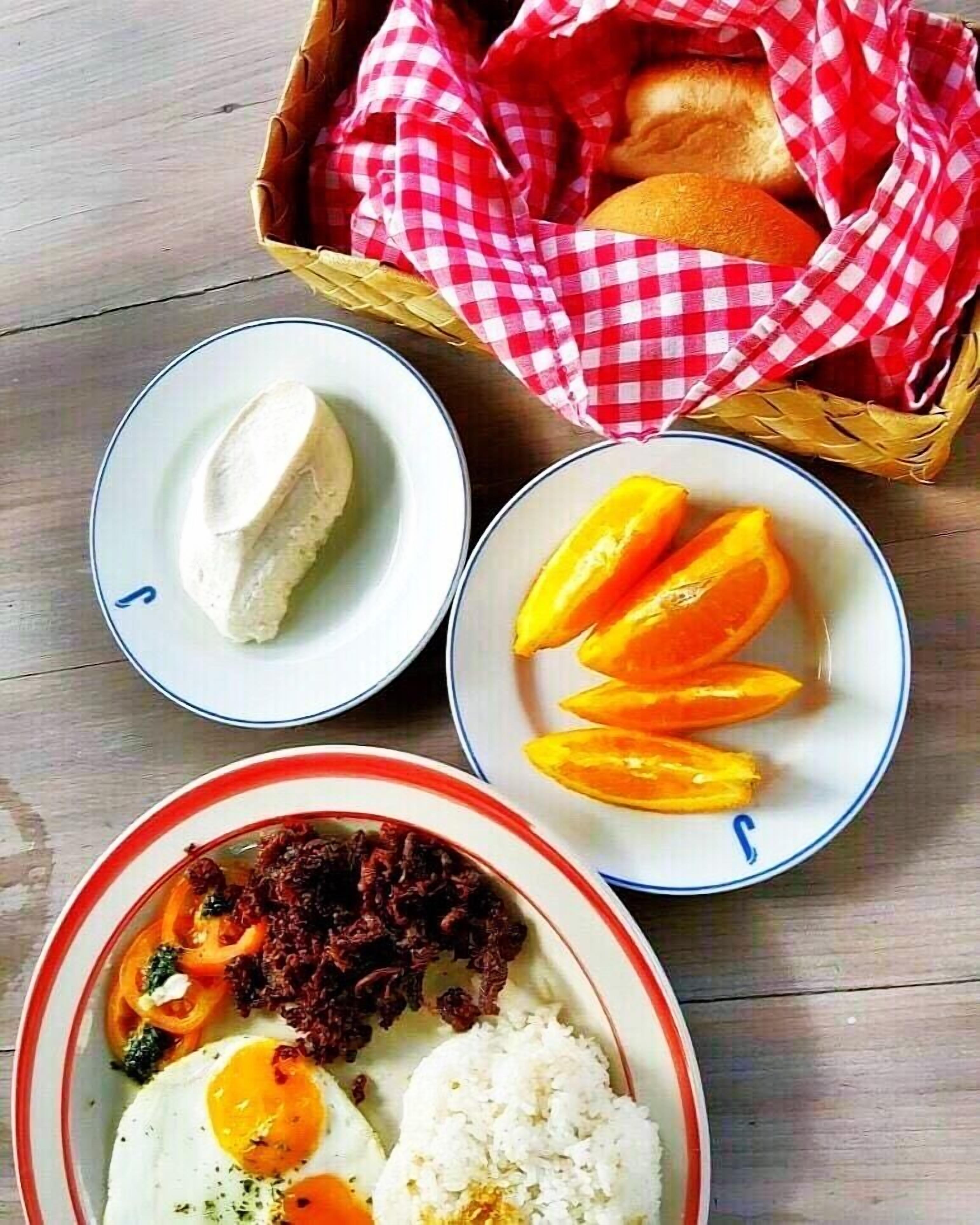 Uma mesa com três pratos: uma tigela de arroz com ovo e vegetais, um prato de manga fatiada e uma tigela que parece ser sobremesa ou acompanhamento.