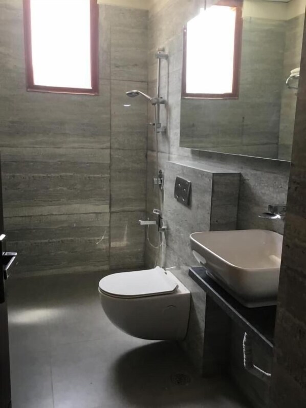 Casa de banho compacta com sanita, lavatório e chuveiro. Há uma janela que proporciona luz natural e um espelho sobre o lavatório.