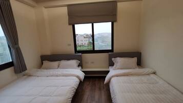 Quarto de hotel com duas camas de solteiro, janela com vista e ventoinha no teto.