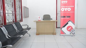 Uma área de recepção com uma mesa de madeira, cadeiras pretas e um grande cartaz promocional da OYO Hotels.