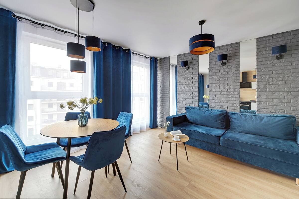 Uma sala de estar moderna com um sofá azul, uma mesa de jantar de madeira com cadeiras e uma pequena mesa lateral.