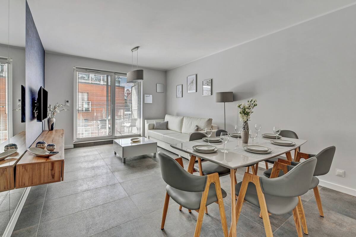 Uma sala de estar moderna com área de jantar, incluindo um sofá, mesa de centro e uma mesa de jantar posta para quatro pessoas.