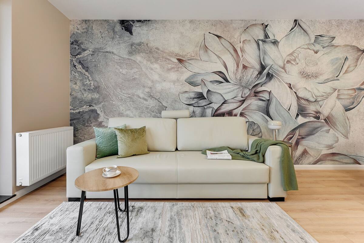 Uma sala de estar moderna com um sofá bege, uma mesa de centro redonda de madeira e um grande mural floral na parede.