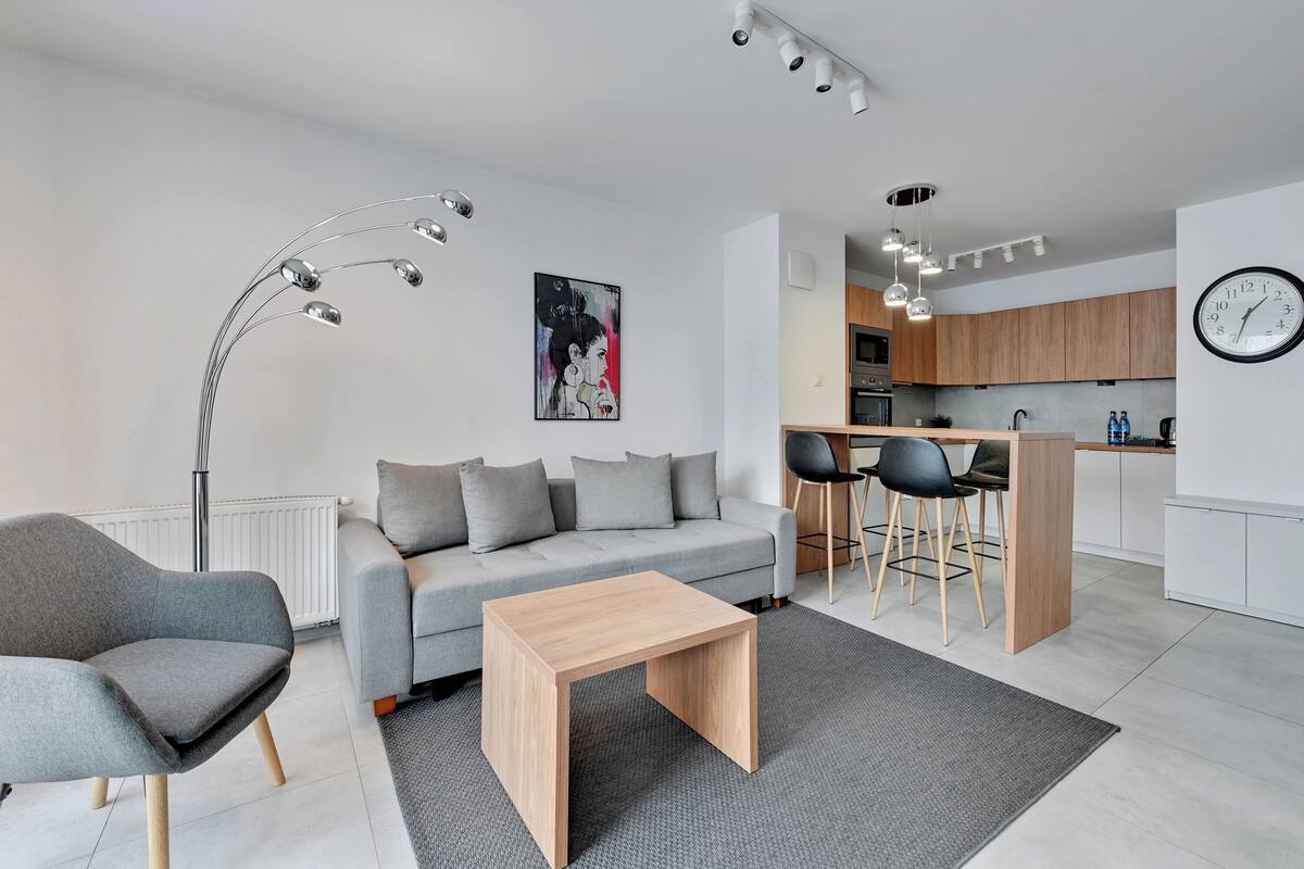 Uma sala de estar moderna com um sofá cinza, uma mesa de centro de madeira e um abajur.