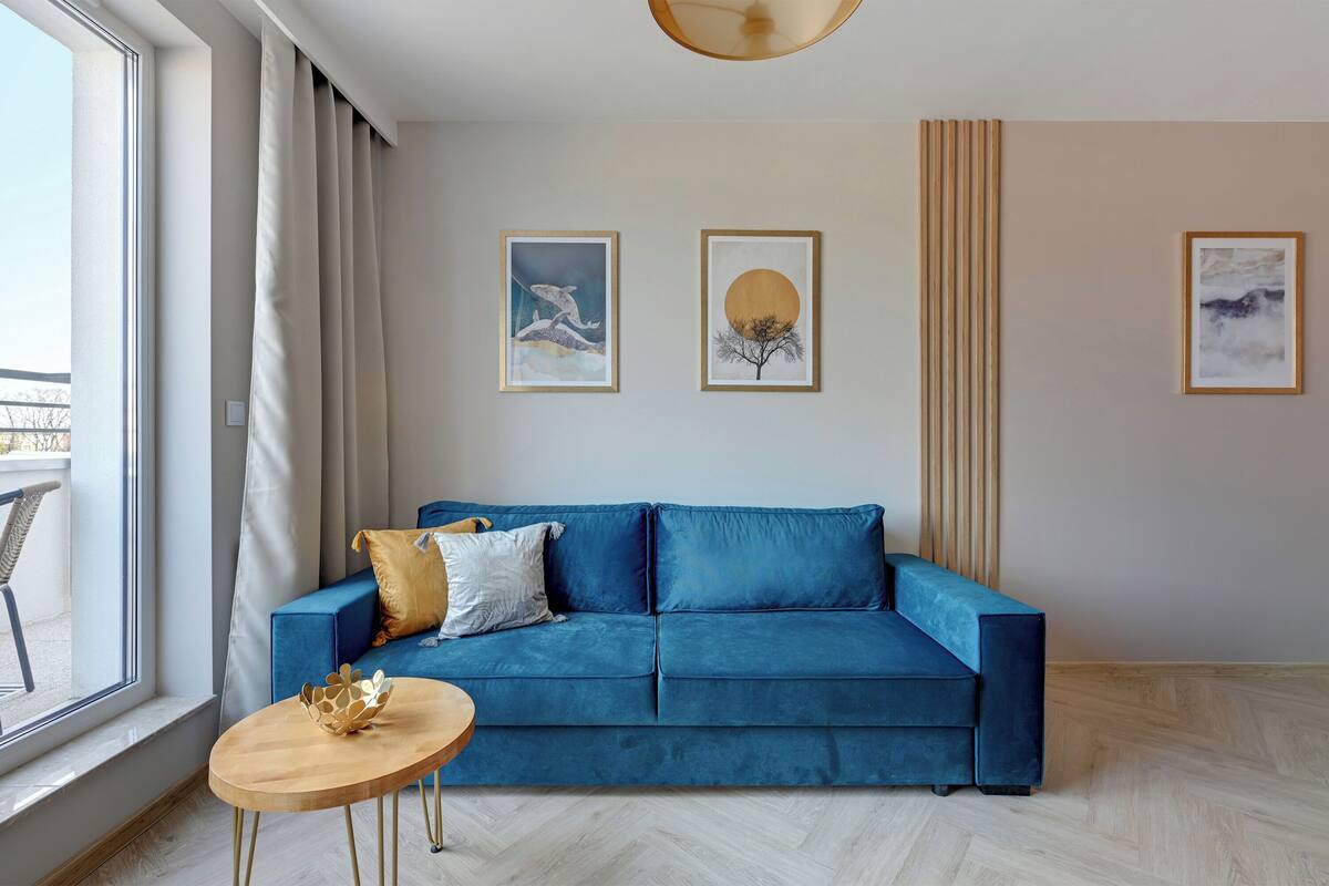 Uma sala de estar moderna com um sofá azul, uma mesa de centro de madeira e três obras de arte emolduradas na parede.
