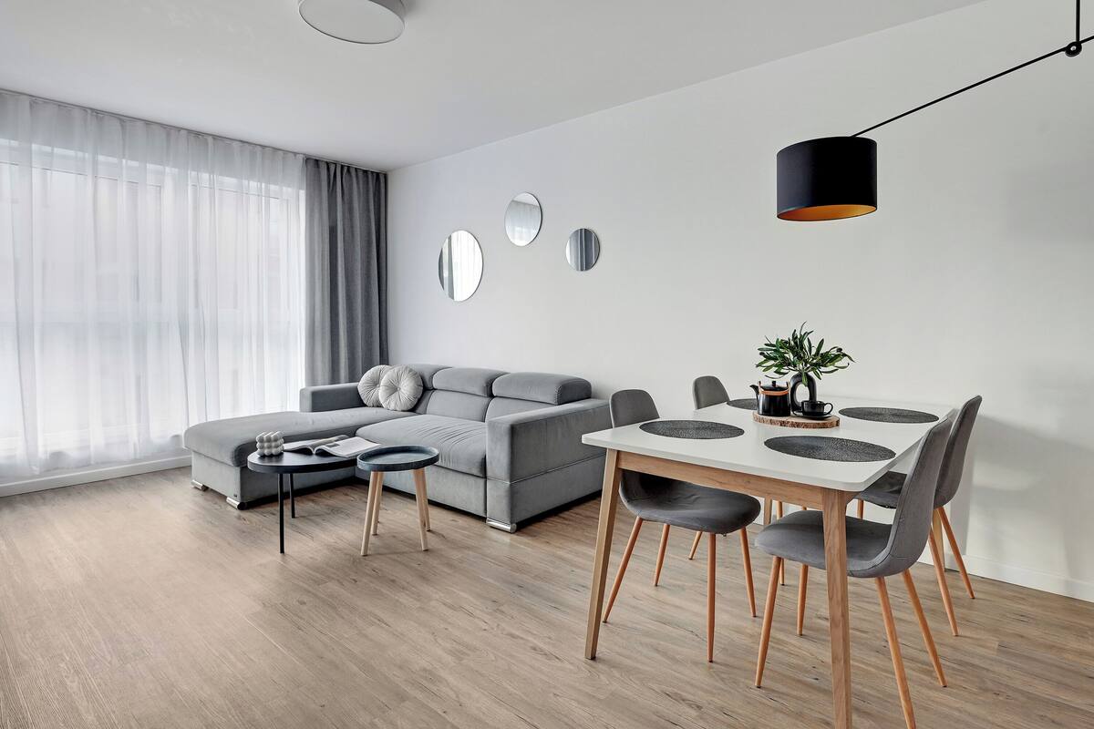 Uma sala de estar moderna com um sofá cinzento, uma mesa de jantar com cadeiras e um candeeiro pendente.