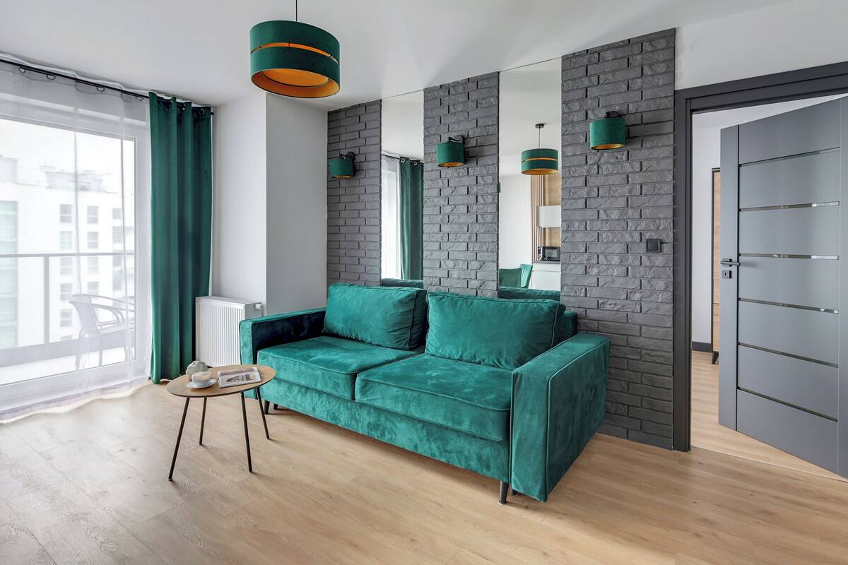 Uma sala de estar moderna com um sofá verde, uma mesinha e uma parede com padrão de tijolos.