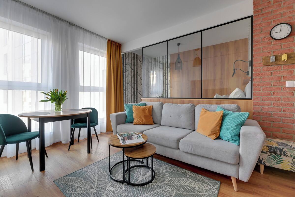 Uma sala de estar moderna com um sofá cinzento, uma mesa de centro redonda e uma mesa de jantar com cadeiras.