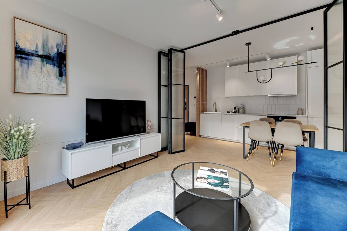 Uma sala de estar moderna com televisão de tela plana, uma mesa de centro de vidro e um sofá azul.