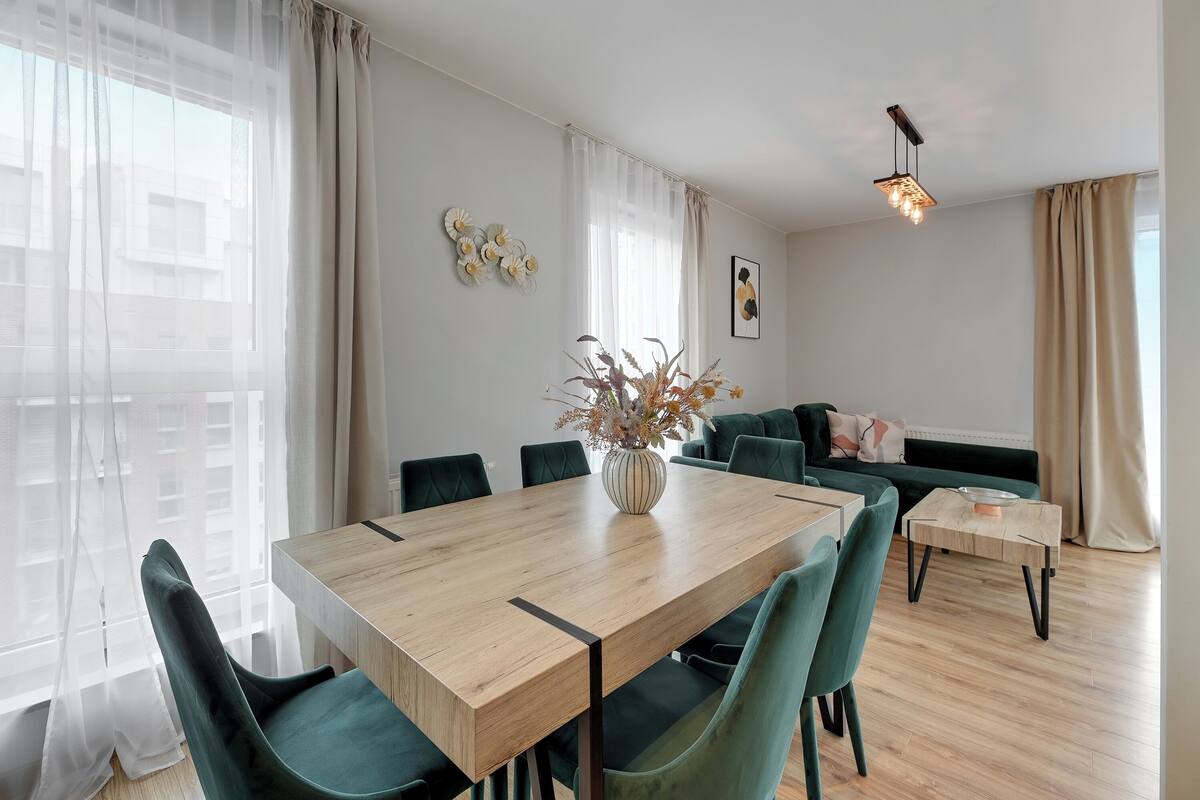 Uma sala de estar moderna com uma mesa de jantar de madeira, cadeiras verdes, um sofá e uma mesa de centro.