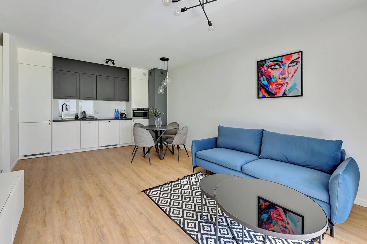 Uma sala de estar moderna com um sofá azul, uma mesa de centro e um espaço de jantar com cadeiras e uma mesa.