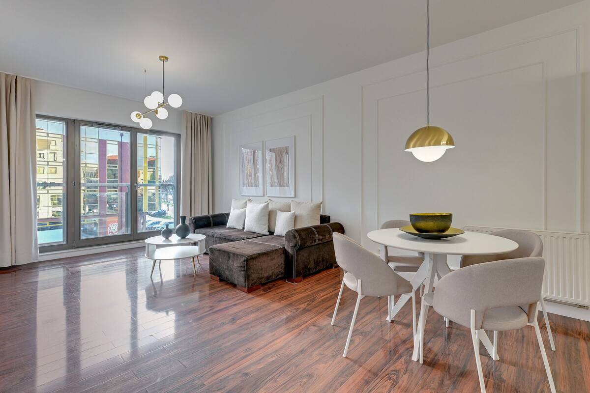 Uma sala de estar moderna com um sofá, uma mesa de jantar com cadeiras e uma janela grande com cortinas.