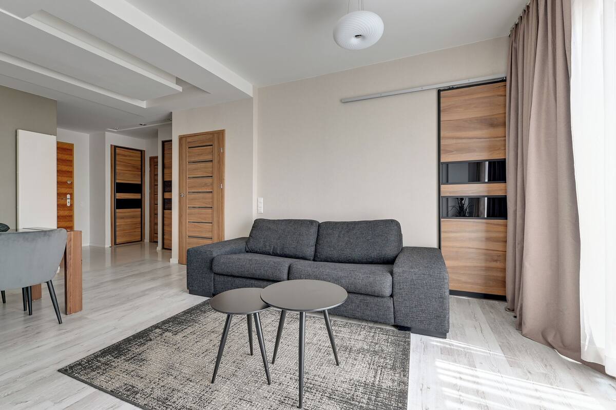 Uma sala de estar moderna com um sofá cinzento, duas mesas redondas e um armário de madeira.