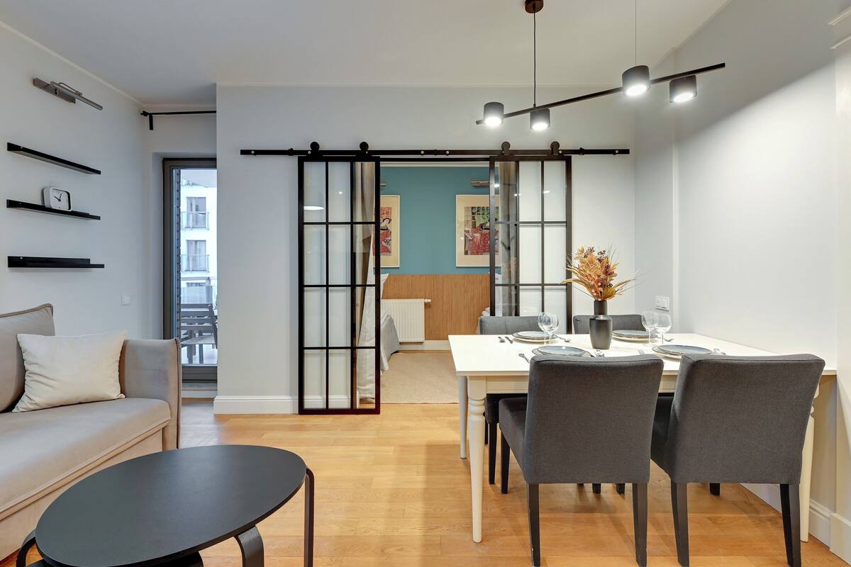 Uma sala de estar moderna com um sofá, uma mesa de jantar com cadeiras e uma porta deslizante que dá para uma varanda.