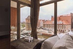 Quarto de hotel com uma grande janela com vista para um canal e edifícios históricos.