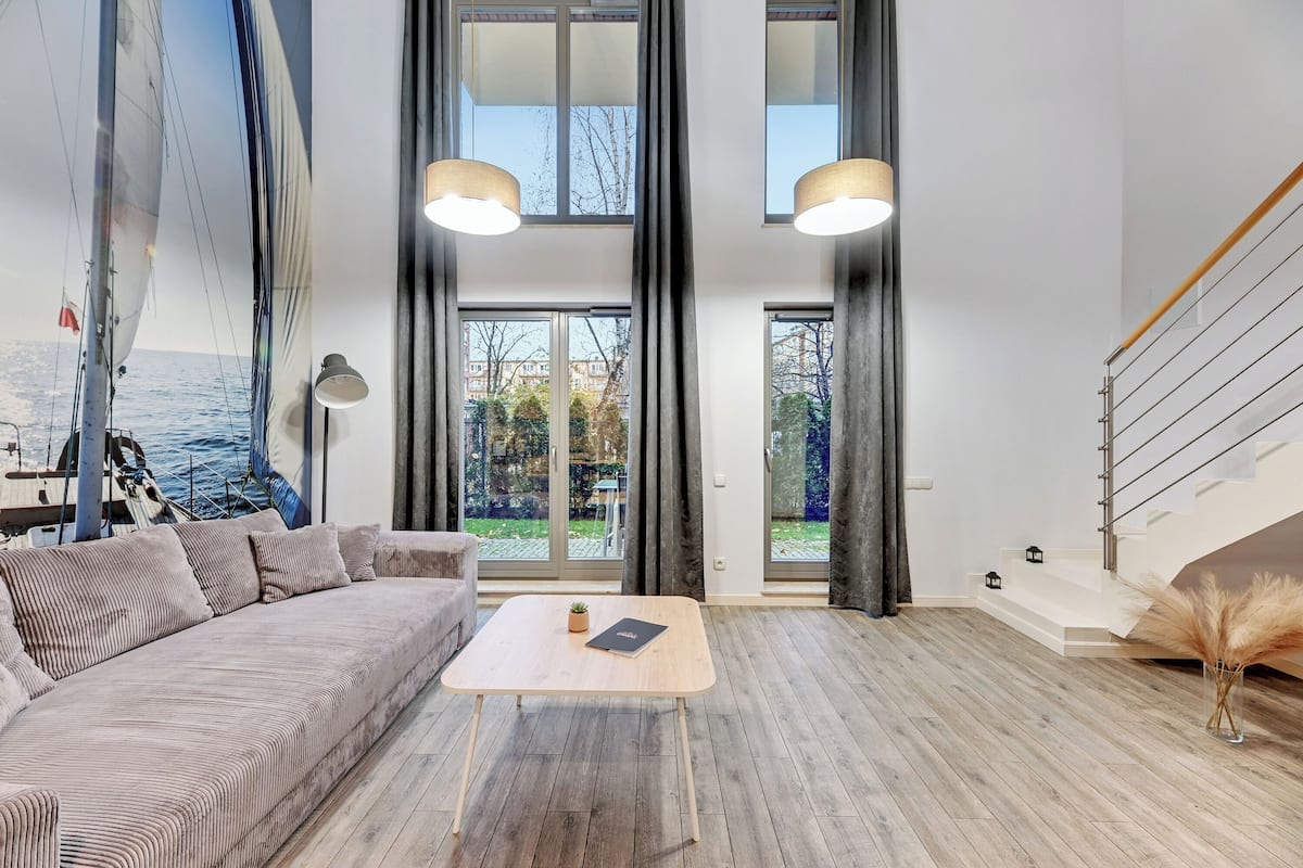 Uma sala de estar moderna com uma janela grande, um sofá, uma mesa de centro e uma escada.