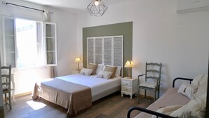 Quarto com cama, duas mesas de cabeceira, uma cadeira, janela com cortinas e luminária geométrica.