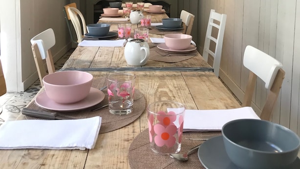 Uma sala de jantar com uma mesa de madeira preparada para quatro pessoas, rodeada de cadeiras.
