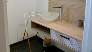 Um banheiro moderno com toucador de madeira, pia de vidro, espelho e folhas decorativas na parede.