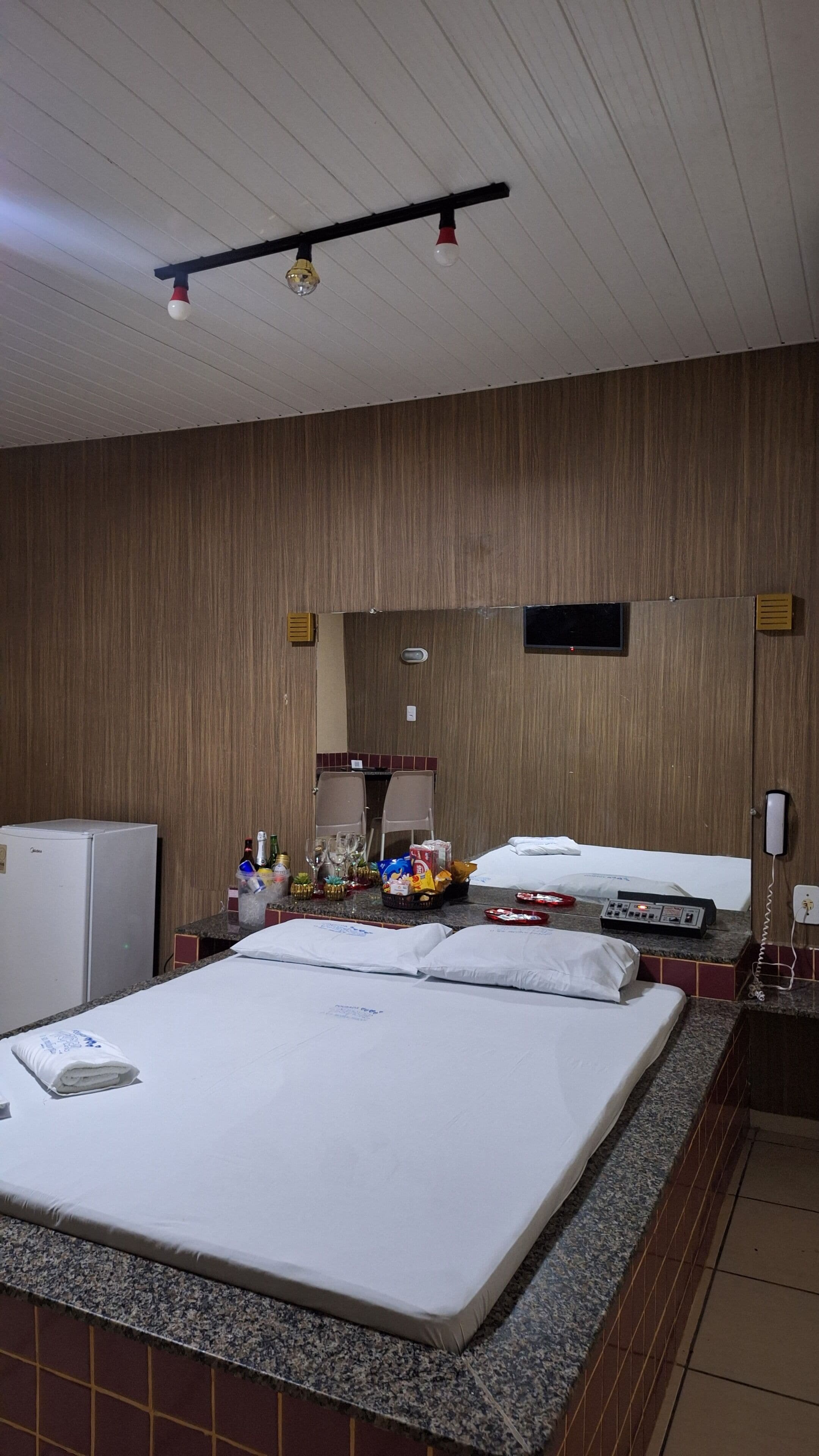 Quarto de hotel com cama, pequeno frigorífico, secretária com cadeira, televisão e telefone.