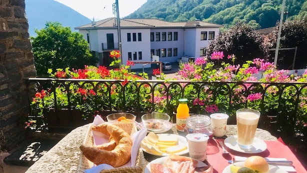 Mesa posta com itens de café da manhã, incluindo croissants, queijo, presunto e frutas, com vista panorâmica para as montanhas ao fundo.