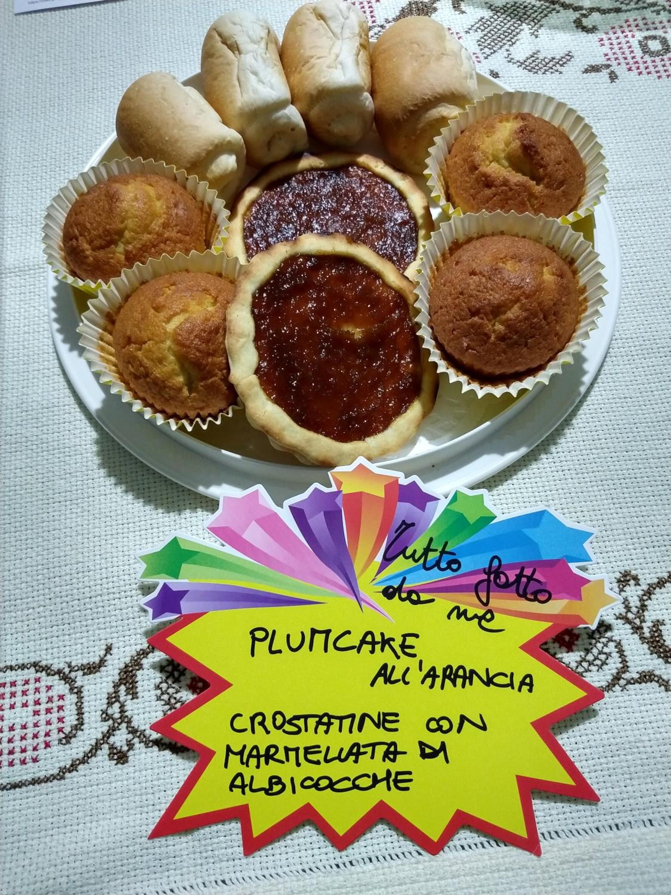 Um prato de doces, incluindo muffins e um bolo de ameixa, com uma placa colorida à frente.