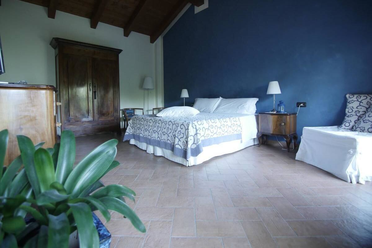 Quarto com cama, mesas de cabeceira, um guarda-roupa de madeira e uma planta em vaso.