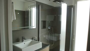 Uma casa de banho moderna com um espelho grande, lavatório e zona de duche.