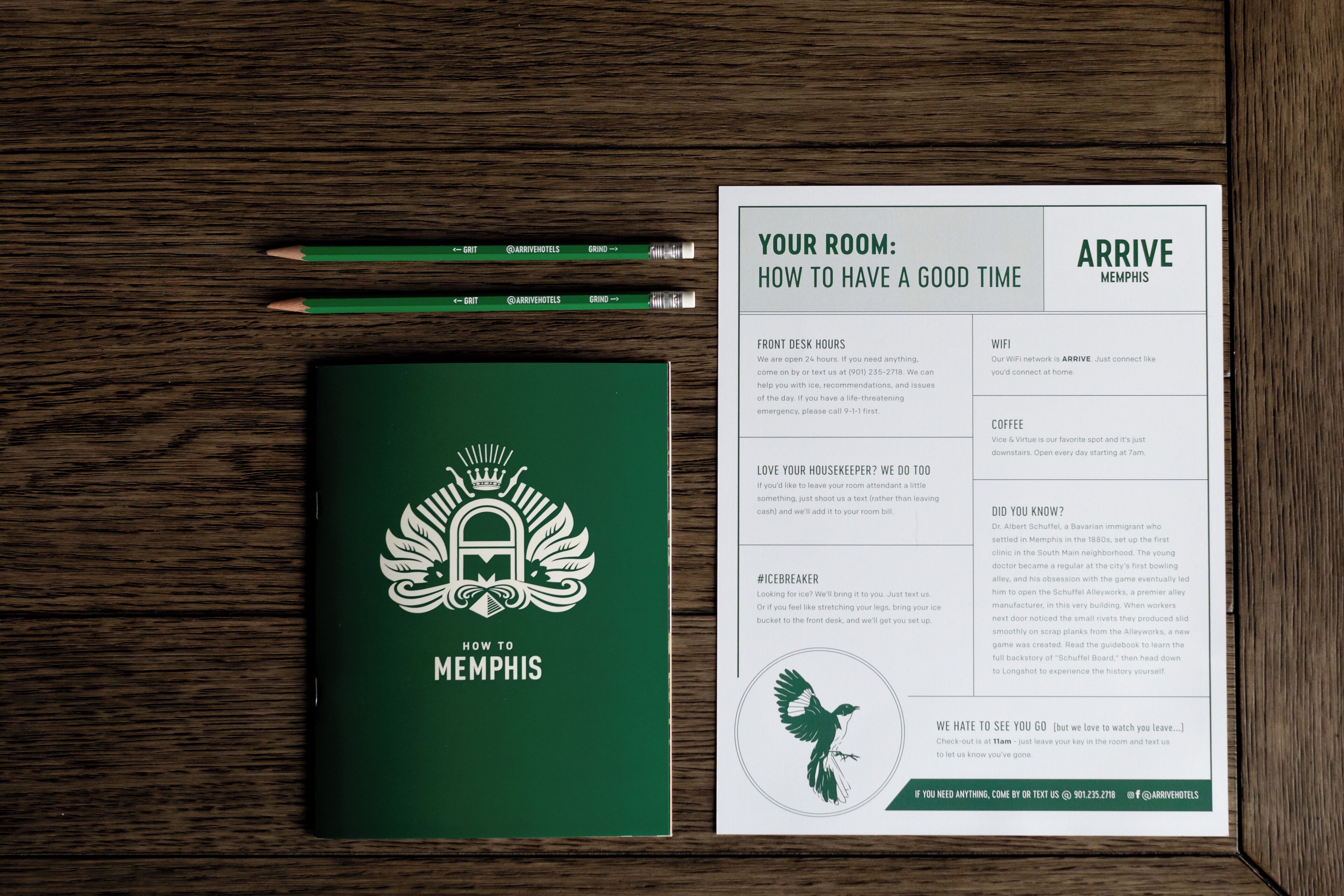 Um livreto verde com o título 'How to Memphis' e um cartão de informações do hotel sobre uma superfície de madeira.