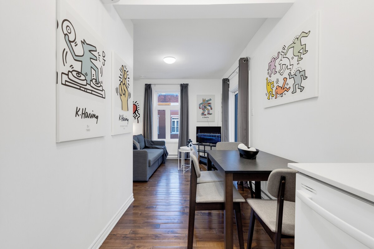 Uma sala de estar moderna com um sofá, uma mesa de jantar com cadeiras e obras de arte nas paredes.