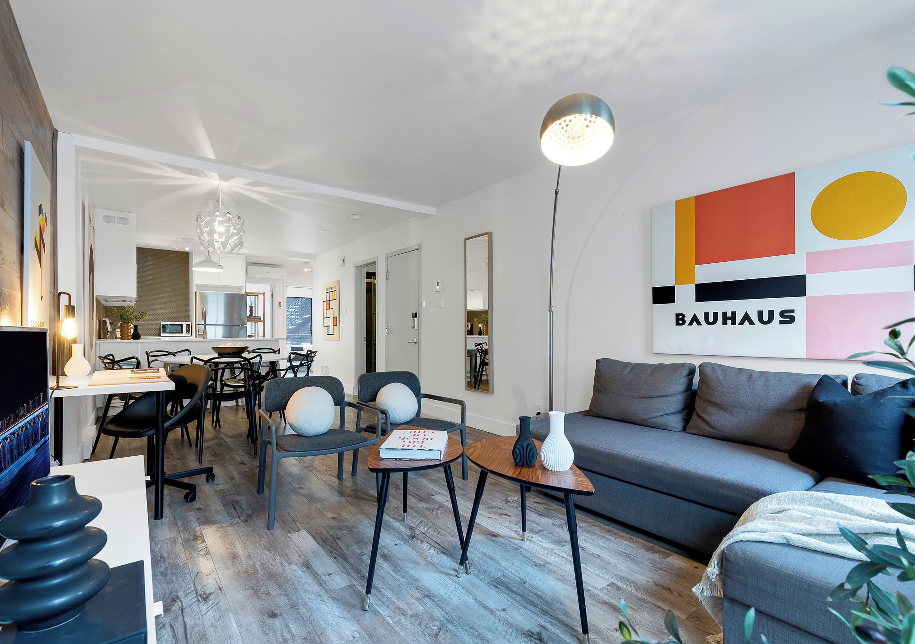 Uma sala de estar moderna com um sofá, cadeiras, um espaço de refeições e uma cozinha ao fundo.